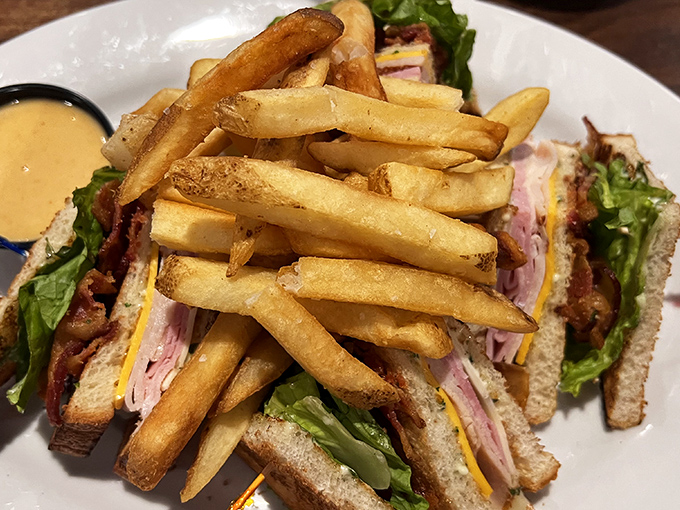 The club sandwich in its final form: architectural perfection with layers of meat, cheese, and veggies, flanked by golden fries standing at attention.
