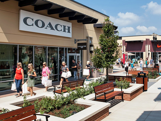 Coach's elegant storefront sits amid thoughtfully designed landscaping. Those benches aren't just decorative&mdash;they're relationship savers during marathon shopping sessions.