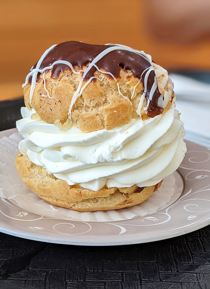 Behold the cream puff in its natural glory &ndash; a golden, chocolate-drizzled dome atop a cloud of whipped cream. Architecture this perfect deserves its own ZIP code.