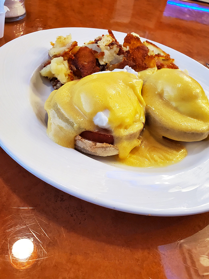Behold the holy grail of breakfast: Eggs Benedict with hollandaise so golden it deserves its own Fort Knox, accompanied by home fries worth fighting over.