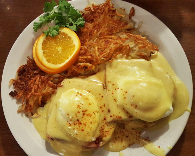 Behold the star of the show: Eggs Benedict draped in hollandaise that cascades like a golden waterfall over perfectly poached eggs. Those hash browns deserve their own fan club.