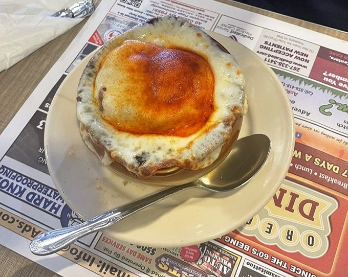 Behold the star attraction! The French onion soup arrives like a bubbling cauldron of comfort, its golden cheese dome glistening with promise.
