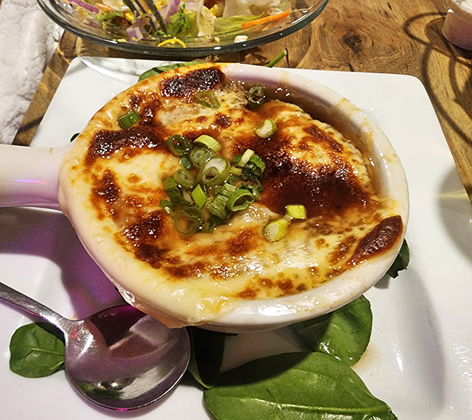 The legendary French onion soup arrives like a bubbling cauldron of comfort, crowned with a golden cheese canopy worth breaking all your diet promises for.