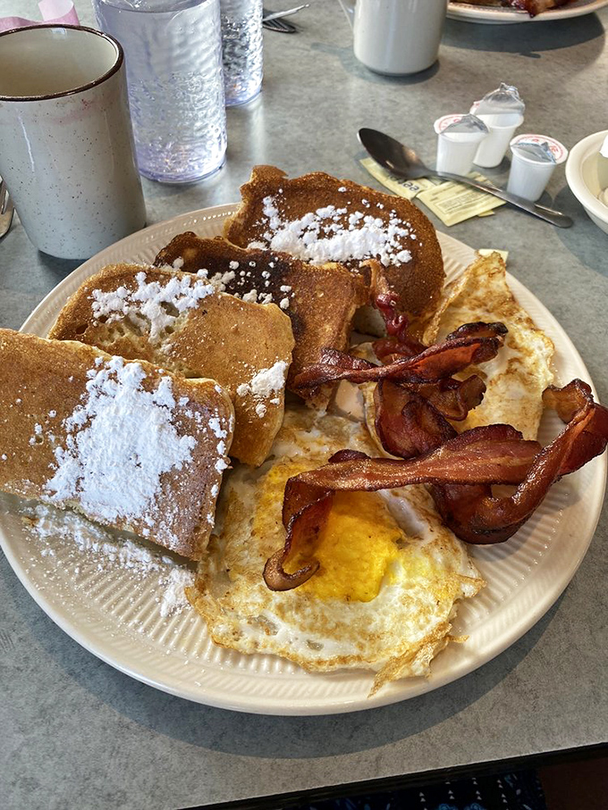 Behold the star attraction: golden-brown French toast dusted with powdered sugar, accompanied by perfectly crisp bacon and sunny-side-up eggs.