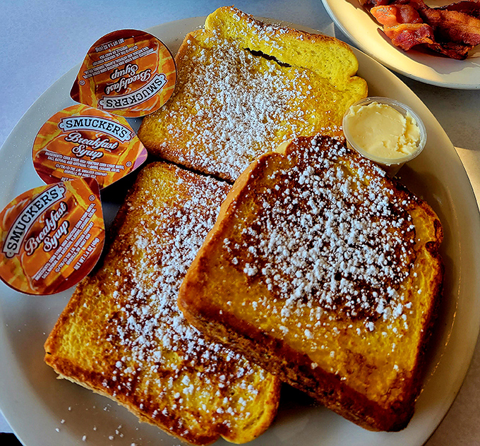 The French toast arrives like a golden revelation&mdash;perfectly crisp exterior giving way to custardy interior, with powdered sugar falling like the gentlest snowfall.