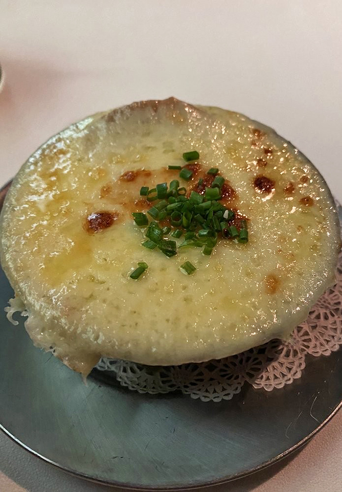 The French onion soup arrives like a bubbling cauldron of comfort, its golden cheese cap waiting to be breached by your eager spoon.