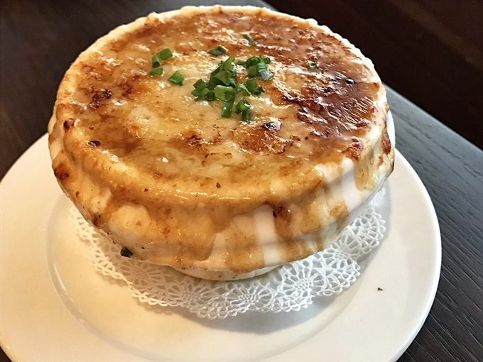 The legendary French onion soup arrives with a crown of perfectly browned cheese that stretches with each spoonful, making you temporarily forget your table manners.