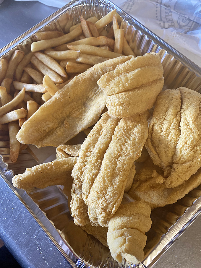 Golden catfish fillets nestled beside fries like edible treasure, each piece wearing its cornmeal coat with crispy pride.