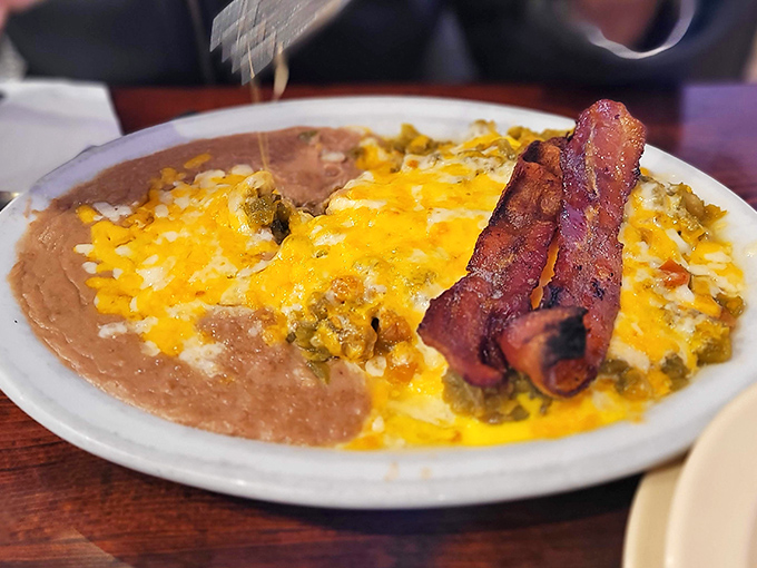 Breakfast nirvana achieved: eggs draped in green chile sauce with melted cheese and bacon standing at attention. This plate doesn't just break your fast&mdash;it demolishes it with flavor.