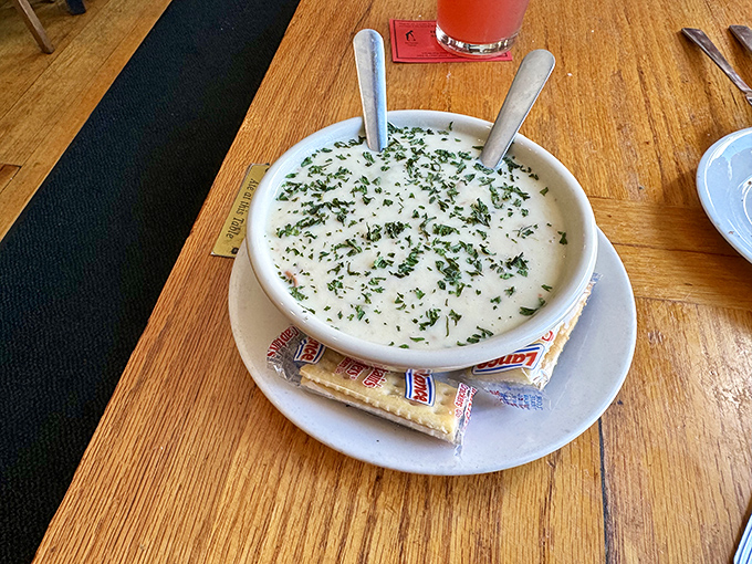 A bowl of creamy soup garnished with fresh herbs arrives like a warm hug from the sea, complete with crackers for dunking.