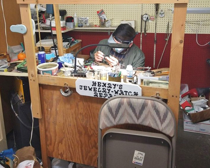 A craftsman at work in his jewelry repair kingdom. Like a surgeon with tiny tools, he breathes new life into timepieces while customers browse nearby.