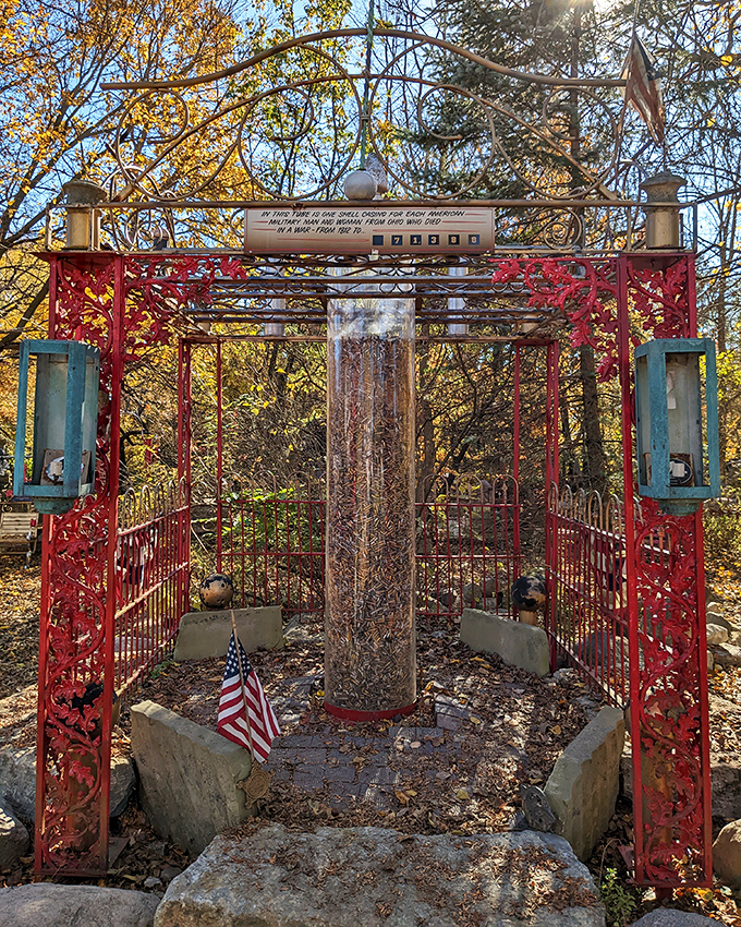 A vibrant red gateway frames a memorial column, creating a moment of reflection. Fall foliage adds nature's perfect complementary colors.