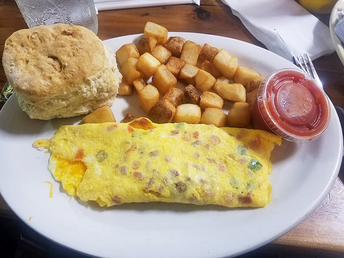 Behold the holy trinity of breakfast perfection: a fluffy omelet, golden country potatoes, and a biscuit that could make a grown person weep.
