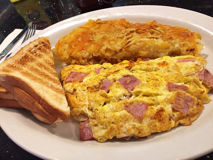 This omelet arrives looking like sunshine on a plate, with ham playing peek-a-boo through layers of fluffy perfection.