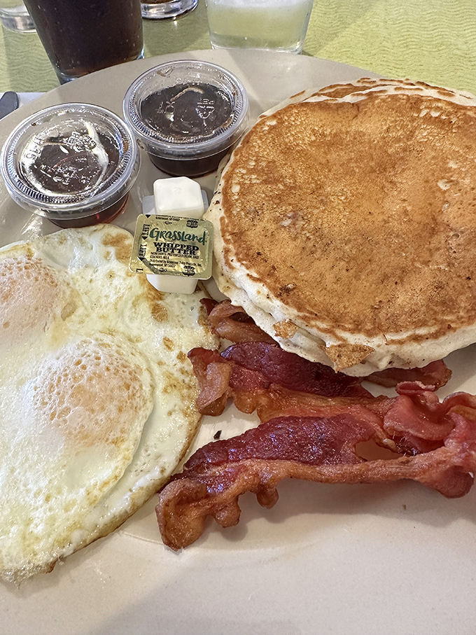 Behold the breakfast trinity: golden pancake, perfectly fried eggs, and bacon that should win some kind of Nobel Prize for pork achievement.