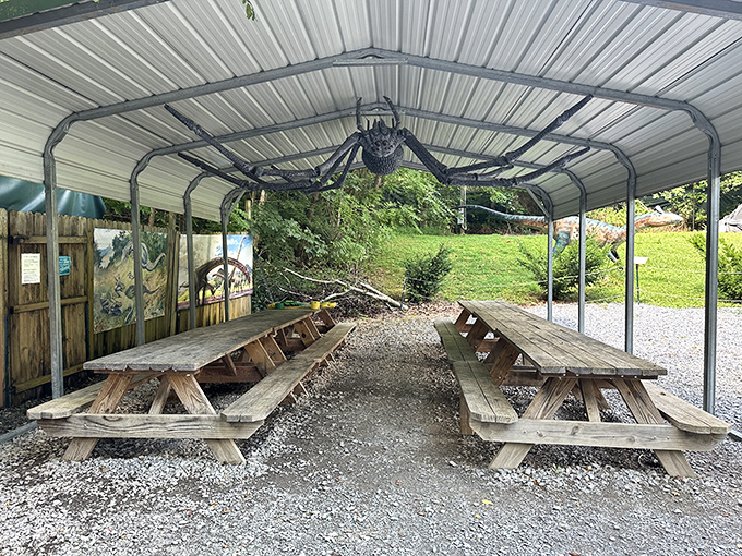 A covered picnic area with wooden tables sits beneath a massive spider decoration, combining prehistoric themes with Halloween fun for hungry explorers.