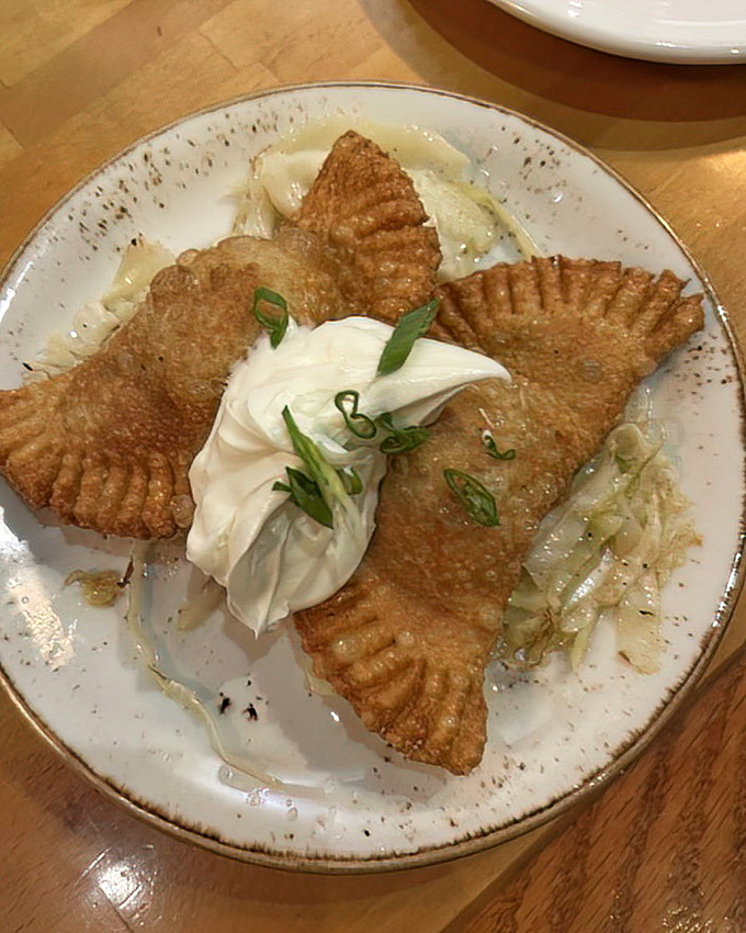 Golden-brown pierogi perfection! These pockets of aged cheddar joy, topped with buttered cabbage, sour cream, and scallions, are worth crossing state lines for.