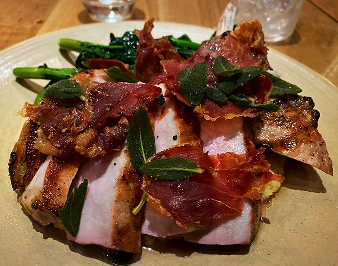 The legendary pork chop arrives like a work of art—perfectly seared, adorned with crispy prosciutto and fresh herbs that'll haunt your dreams.