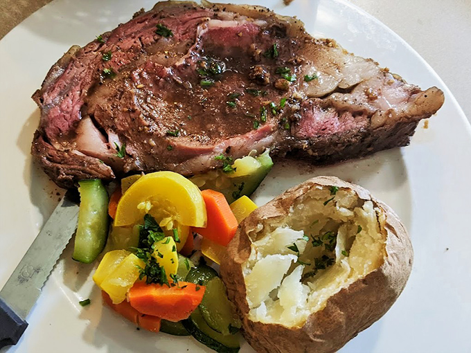 Behold the star attraction: prime rib cooked to perfection, accompanied by fresh vegetables and a loaded baked potato that's practically begging to be devoured.