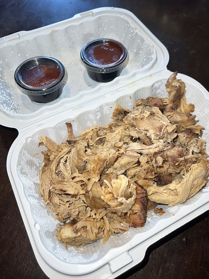 Pulled pork so tender it practically surrenders to your fork. Those two sauce cups aren't just condiments&mdash;they're flavor companions for the journey.