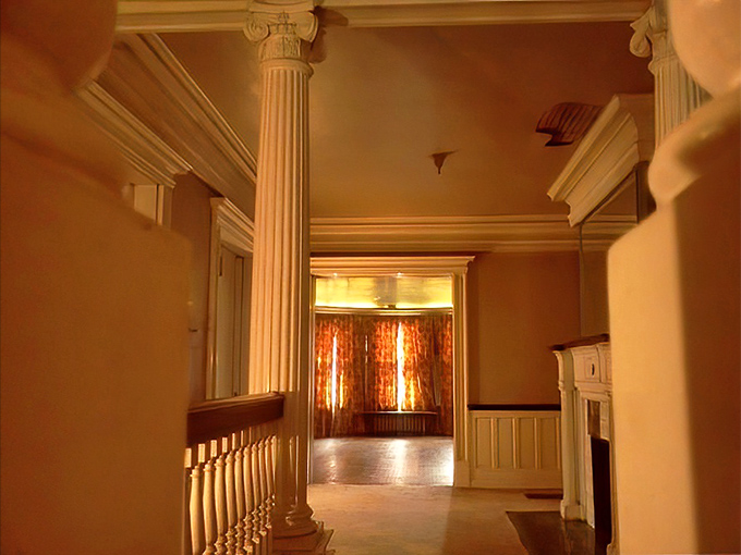 Classical columns frame the entryway like sentinels guarding the past, while sunlight streams through distant windows, illuminating pathways to other eras.