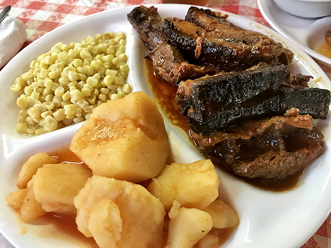 The legendary roast beef arrives with perfect bark and tender interior, flanked by golden corn and potatoes swimming in savory juices.