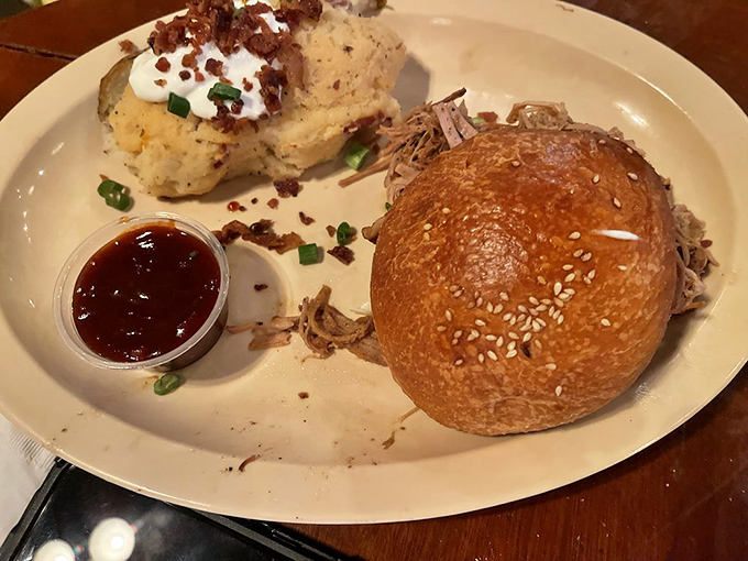 The pulled pork sandwich arrives like a savory work of art, accompanied by a loaded baked potato that's practically a meal itself.