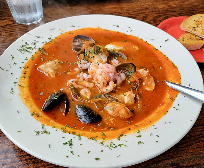 The Seafood Stew arrives like a sunset-colored ocean in a bowl, where plump shrimp and tender mussels play hide-and-seek in a tomato broth that's been simmering with secrets.
