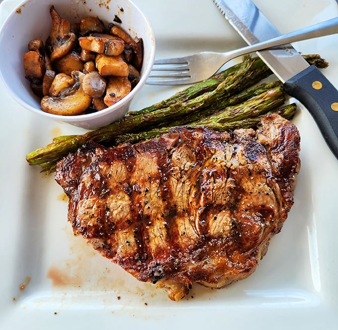 Behold the ribeye in its natural habitat &ndash; perfectly charred, resting beside grilled asparagus and saut&eacute;ed mushrooms. This is meat's highest calling.
