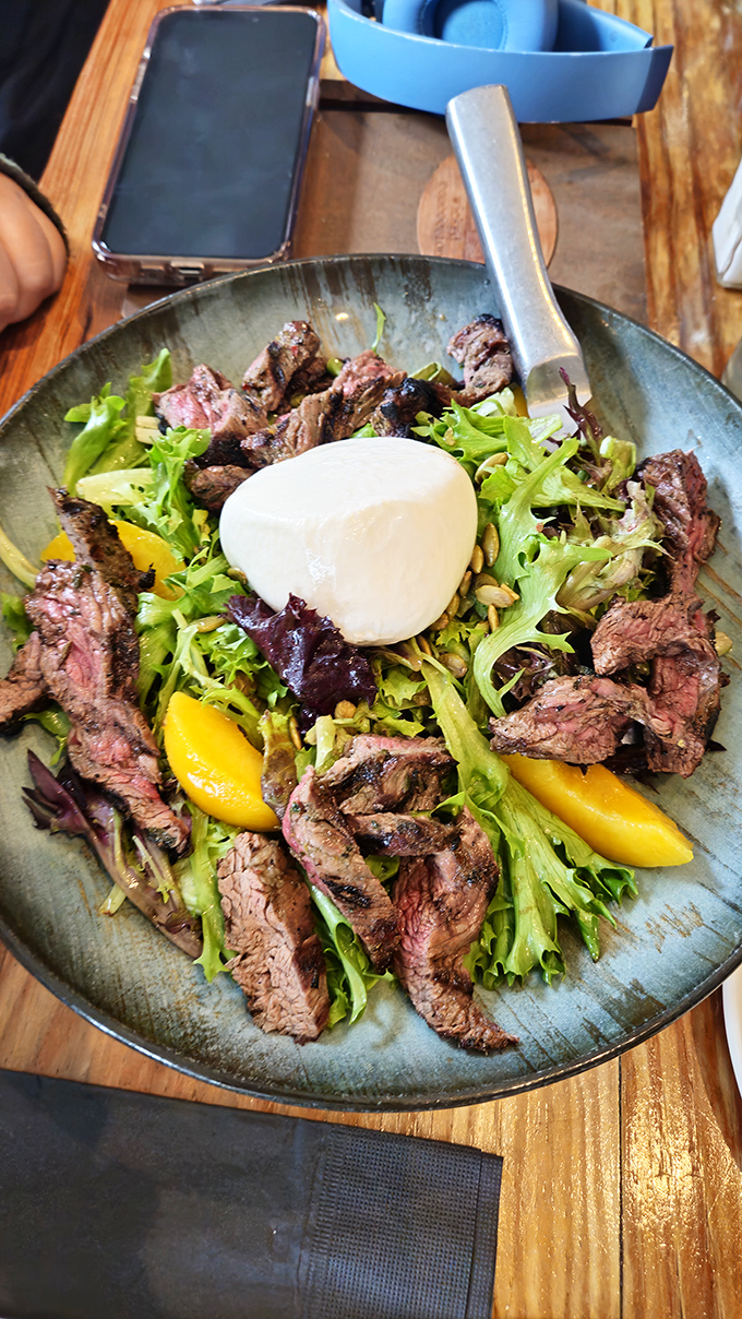 The legendary steak salad in all its glory. Perfectly medium-rare beef, vibrant greens, and that poached egg waiting to create its own luxurious dressing.