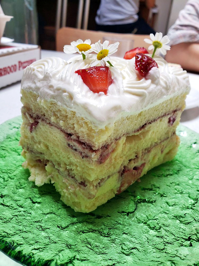 The slab cake in its natural habitat: adorned with fresh strawberries and daisies, layers visible like geological strata of deliciousness.