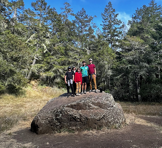 A family celebrates their summit conquest atop a trail boulder&mdash;the universal "we made it" pose that's mandatory in hiking circles.