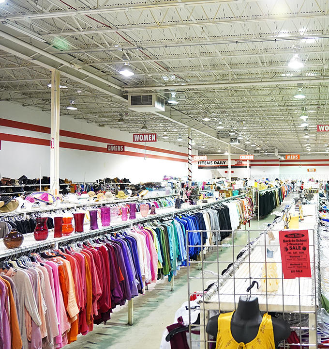 
A rainbow of garments stretches toward the horizon. The "Women" signs overhead serve as beacons guiding shoppers through this sea of secondhand fashion.