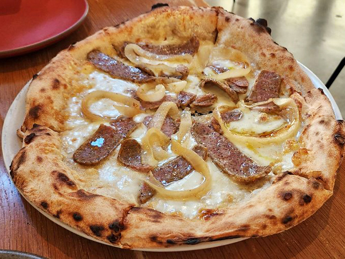 The Wiseguy pizza arrives like a beautiful contradiction: rustic yet refined, with wood-roasted onions and fennel sausage playing harmony to smoked mozzarella's melody.