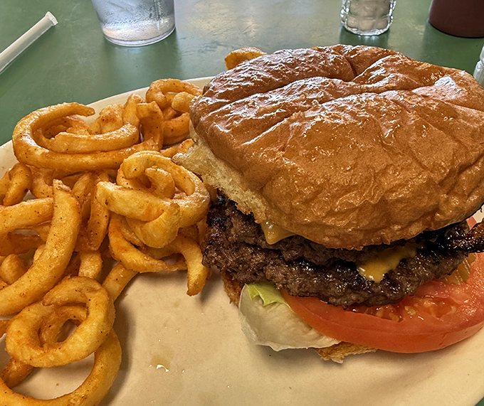 Behold the star of the show: a cheeseburger so perfectly constructed it deserves its own architectural award. Those curly fries are just showing off.