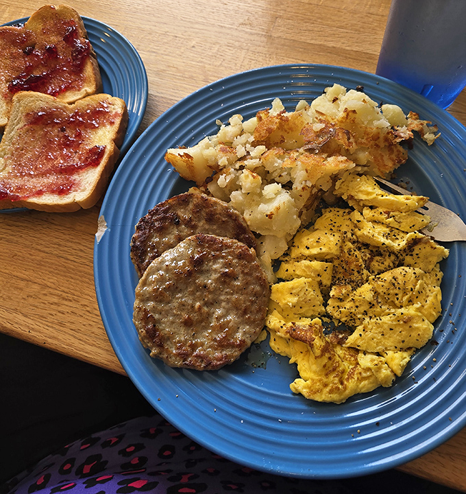 Breakfast perfection on a blue plate: perfectly scrambled eggs, seasoned home fries, and toast with just the right amount of jam.