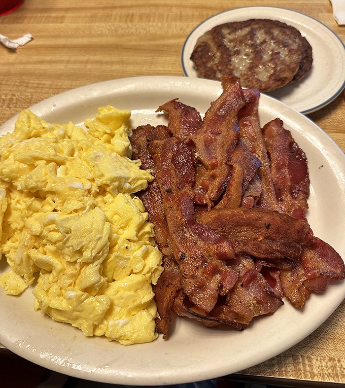 Breakfast of champions! Golden scrambled eggs and bacon cooked to that perfect sweet spot between crisp and chewy. That sausage patty deserves its own fan club.