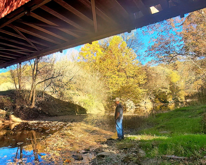 Beneath the bridge's protective embrace, the creek continues its timeless journey, indifferent to the human engineering above.