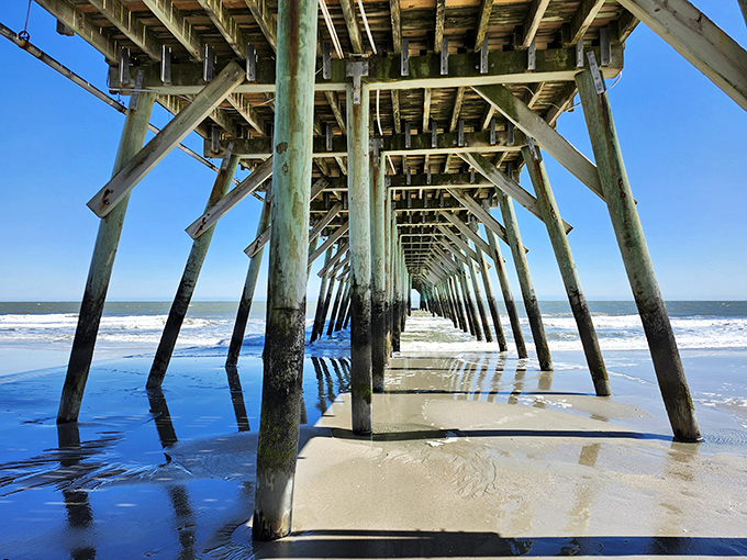 Beneath the pier, a geometric wonderland of supports creates nature's cathedral. Architecture meets ocean in this mesmerizing perspective.