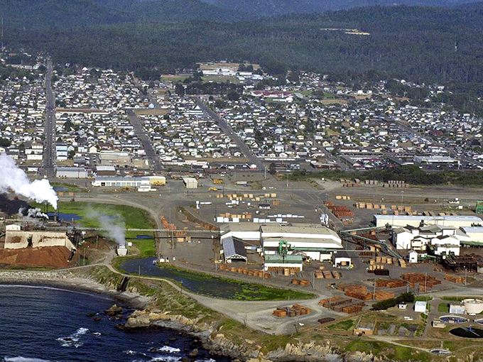 The town's industrial past is visible in this aerial view, where lumber operations once dominated the coastline before nature reclaimed her throne.