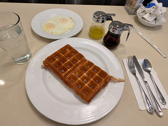 The Belgian waffle arrives golden and grid-perfect, like a delicious spreadsheet ready to calculate your happiness with every syrup-soaked square.