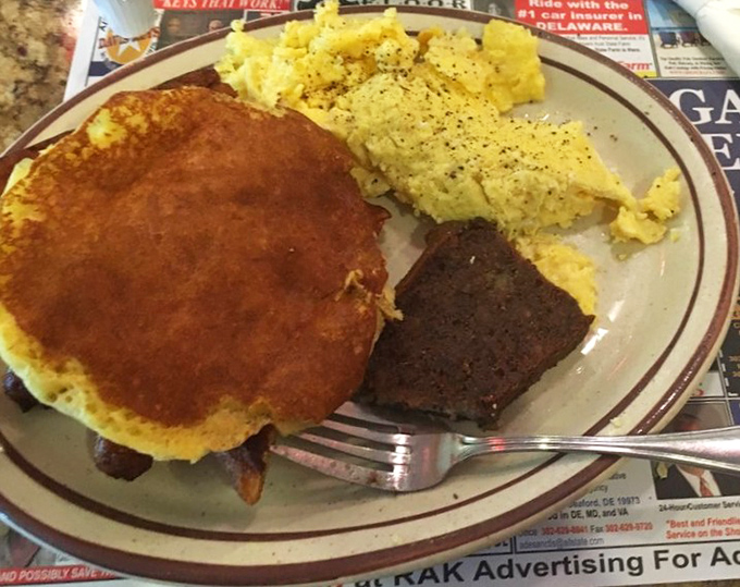 A hearty breakfast plate featuring a golden pancake, scrambled eggs, and scrapple &ndash; Delaware's morning trilogy of deliciousness that fuels the entire day.