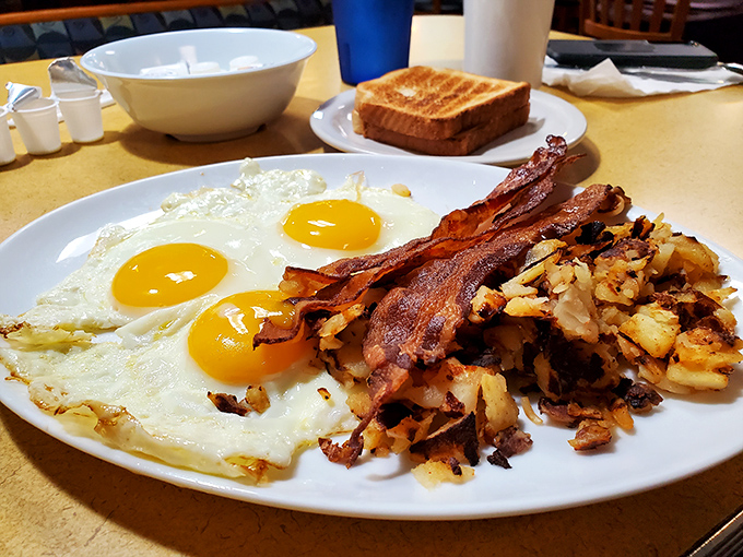 The classic American breakfast trifecta: perfectly crisp bacon, golden eggs, and home fries that somehow taste better with aviation in view.