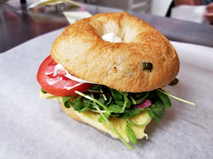 This isn't your sad drive-thru breakfast sandwich. It's a proper morning masterpiece with fresh bagel, egg, greens, and tomato that makes Monday feel like Friday.