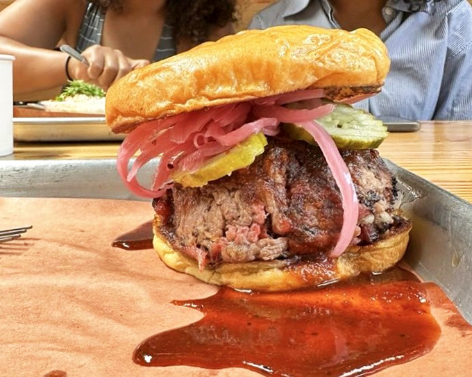 Architecture of deliciousness: smoked brisket, pickled onions, and sauce on a fresh bun. This sandwich doesn't need a building permit to construct flavor.