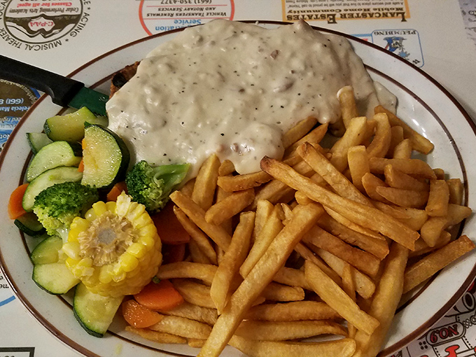 The star of the show: chicken fried steak with crispy edges and creamy gravy, accompanied by fries and vegetables pretending to make it healthy.