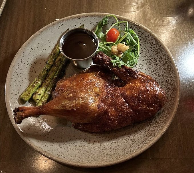 The half crispy duck arrives like royalty, its golden-brown skin glistening with promise alongside perfectly grilled asparagus.