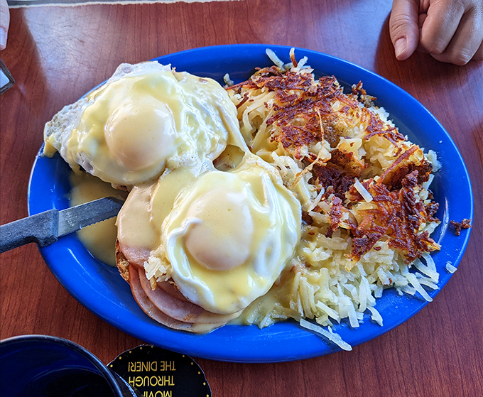 Eggs Benedict done diner-style: perfectly poached eggs lounging on ham like they're at a spa retreat, blanketed in hollandaise and surrounded by crispy hash browns.