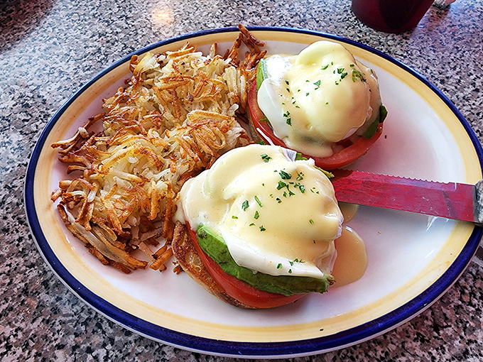 Eggs Benedict with avocado and tomato&mdash;where hollandaise sauce cascades like a buttery waterfall and hash browns achieve that perfect crisp-to-fluffy ratio.