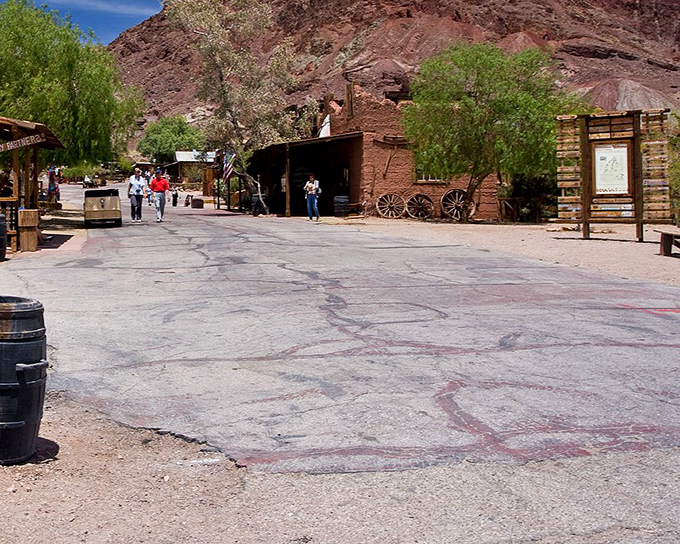 Rustic adobe buildings frame the walkway into town. The trees offer rare shade in this landscape where even cacti need to bring their own sunscreen.